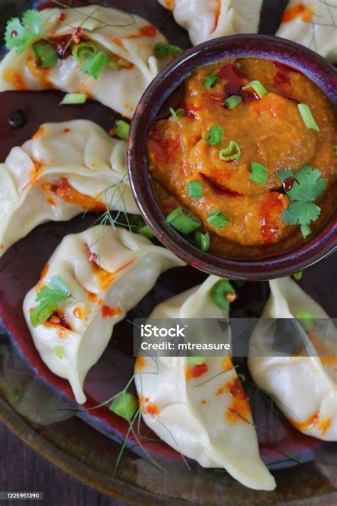 찐 모모 닭고기와 혼합 야채로 채워진 흰 밀가루와 물 반죽 칠리 오일이 뿌려진 오렌지 매운 디핑 소스의 라메킨을 둘러싼 접시에 올려진 모습 높은 전망 램킨에 대한 스톡 사진