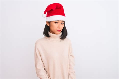 고립 된 흰색 배경 위에 크리스마스 산타 모자를 쓰고 있는 젊은 아름다운 중국 여성은 우울하고 고민에 대해 걱정하고 화가 나서 두려워합니다 슬픈 표정 12월에 대한 스톡