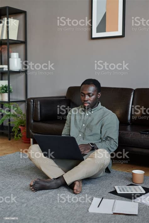 노트북을 사용하여 금융 프로젝트에 종사하는 거실에서 바닥에 앉아있는 젊은 흑인 남성의 수직 샷 20 24세에 대한 스톡 사진 및 기타 이미지 Istock