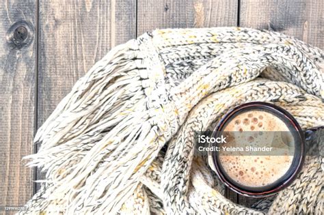 따뜻한 니트 울 스카프에 싸여 소박한 나무 테이블 배경에 거품이있는 뜨거운 커피컵 카푸치노 머그잔 겨울 열 휴일 및 이벤트의 개념 맨 위 보기입니다 0명에 대한 스톡 사진