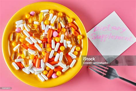 대체 의학의 개념입니다 분홍색 배경에 포크를 가진 노란 격판덮개에 있는 캡슐 양분 정제 및 환 약에 있는 비타민 스티커에 비문 식이 보조 제 0명에 대한 스톡 사진 및 기타