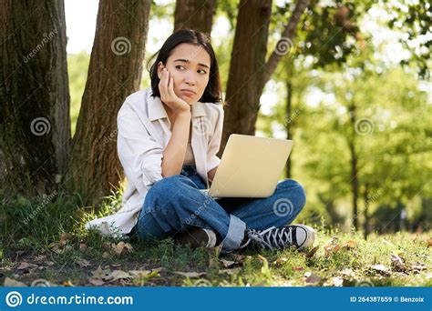 Portrait Of Young Asian Woman Sitting In Park Near Tree Working On Laptop Using Computer