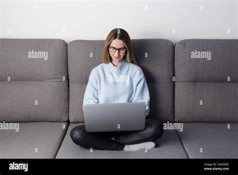Beautiful Blonde Woman Sitting On Couch And Working On Silver Laptop