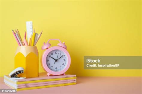 학교 개념으로 돌아 가기 연필 눈금자 알람 시계 노트북과 노란색 벽 배경에 스테이플러가있는 분홍색 책상 펜 홀더에 학교 용품 사진 0명에 대한 스톡 사진 및 기타 이미지