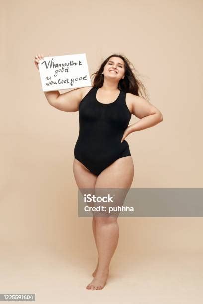 플러스 크기 모델 뚱뚱한 여자 에 검정 바디 수트 전체 길이 초상화입니다 공백에 쓰여진 당신이 잘 생겼다고 생각할 때라는 문구가 적힌 종이를 들고 있는 여성 웃는 몸 긍정적