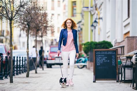 젊은 Redhaired 백인 여자 두 가지 색상의 작은 치와와 품종 개 가죽 끈에 유럽 거리를 따라 산책 흐림 따뜻한가 봄 날씨입니다 여자 가죽 재킷과 핑크 신발 입고