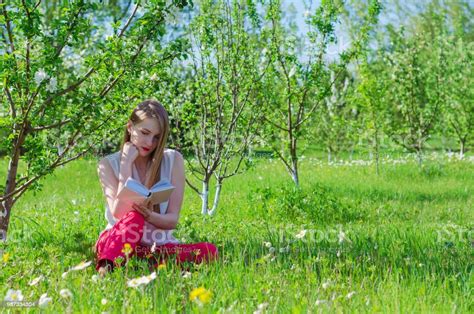 젊은 아주 화창한 날에 꽃이 만발한 사과 나무와 읽기 책 아래 잔디에 앉아 흰 상단과 빨간 바지에 여자 텍스트에 대 한 공간을 복사 개화기에 대한 스톡 사진 및 기타 이미지