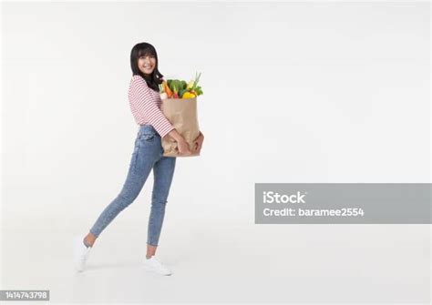 아름다운 미소 짓는 아시아 여성은 식료품으로 가득 찬 쇼핑백을 들고 흰색 배경에 고립 된 공간을 따로 복사하려고합니다 흰색