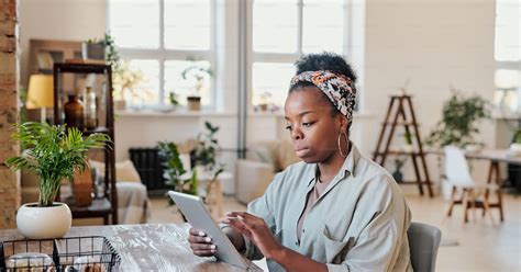 머리 스카프를 두른 진지한 젊은 흑인 여성이 나무 책상에 앉아 열린 공간 사무실에서 온라인 프로젝트를 진행하고 있다 사진