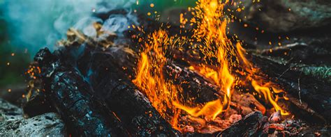 불에 타버린 생생한 연기가 나는 장작이 클로즈업되었습니다 모닥불과 푸른 연기의 주황색 불꽃이 있는 분위기 있는 배경 모닥불의 따뜻한 풀 프레임 이미지 공중에서 빛나는 불씨