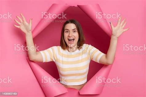 흥분한 행복한 갈색 머리 젊은 성인 백인 여성의 초상화는 분홍색 종이 배경을 깨고 입을 벌리고 팔을 들고 서서 기뻐합니다 20 24세에 대한 스톡 사진 및 기타 이미지