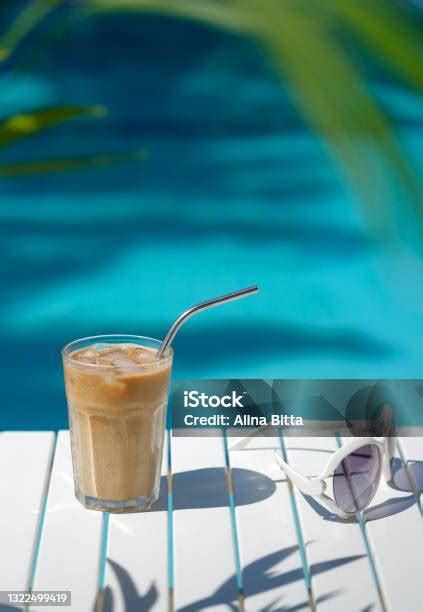 아이스 커피 키프로스 프라페 프레도는 수영장의 푸른 맑은 물에 대해 흰색 테이블에 선글라스와 함께 여름 미니멀 한 배경 휴일 또는 휴가 개념 복사 공간 라떼에 대한 스톡