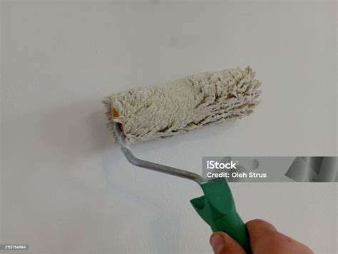 녹색 손잡이가 달린 롤러로 벽을 흰색으로 칠합니다 사진에서 사람의 손은 벽 페인트 롤러를 손에 들고 방의 벽을 흰색으로 칠하고 있습니다 집 수리에 대한 주제 개선에 대한