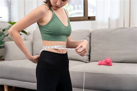 운동복을 입은 스포티한 여성이 허리 둘레를 측정하고 줄자를 보고 있다 20 24세에 대한 스톡 사진 및 기타 이미지 20 24세 가냘픈 거실 Istock