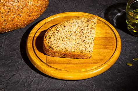 아마 양귀비 씨앗 참깨 기장 호박 해바라기 씨 유리 항아리에 올리브 오일 나무 판 검은 배경 하드 라이트 낮은 키에 사진 소박한 천연 효모가없는 빵의 조각 갈색에 대한 스톡