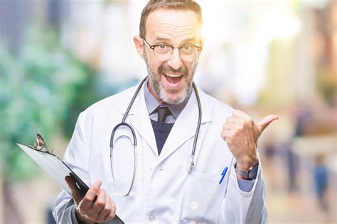 중 년 수석 노인의 의사 남자 고 행복 얼굴 미소와 측면까지 손가락으로 보여주는 격리 된 배경 위에 클립보드를 들고 가리키기에 대한 스톡 사진 및 기타 이미지 Istock