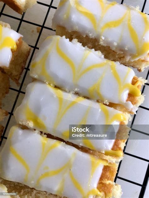 금속 냉각 랙에 흰색 퐁당 아이싱과 깃털 노란색 레몬 맛 장식을 얹은 홈메이드 레몬 트레이 베이크 케이크 슬라이스의 이미지 전경 높은 전망에 초점을 맞추고 0명에 대한 스톡