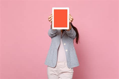 스튜디오에서 분홍색 파스텔 배경에 고립 된 빈 빈 화면 태블릿 Pc 컴퓨터와 얼굴을 덮고 줄무늬 재킷에 젊은 여자 사람들은 진심으로 감정 라이프 스타일 개념입니다 복사