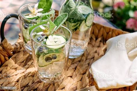 상쾌한 여름 음료 오이가 얼음 세이지 오이 레몬 꽃을 넣은 물을 정원의 테이블에 주입했습니다 신선하고 건강한 감기 해독 음료 피트니스 음료 감귤류 과일에 대한 스톡 사진 및