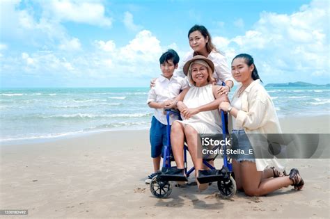 휠체어를 탄 행복한 장애인 노인 여성이 열대 해변에서 가족과 함께 시간을 보내고 있습니다 아시아 할머니 딸과 손자는 여름 휴가에 휴식과 휴식 16 17 살에 대한 스톡 사진