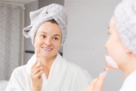 Beautiful Woman Is Getting Massage Face Using Jade Roller In Front Of The Mirror At Home Stock