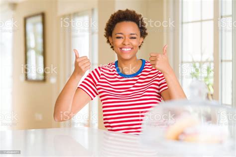 집 성공의 젊은 아름 다운 아프리카계 미국인 여자는 손으로 긍정적 인 제스처를 하 고 웃 고 행복 한 엄지 손가락 쾌활 한