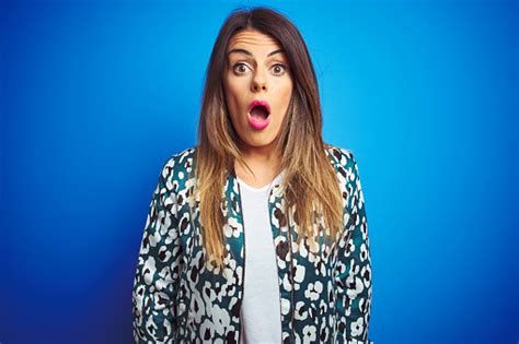 파란색 고립 된 배경 위에 서있는 재킷을 입은 젊은 아름다운 여성은 놀라움의 표정 두려움 흥분된 얼굴로 충격을 받았습니다 쇼크에 대한 스톡 사진 및 기타 이미지 Istock
