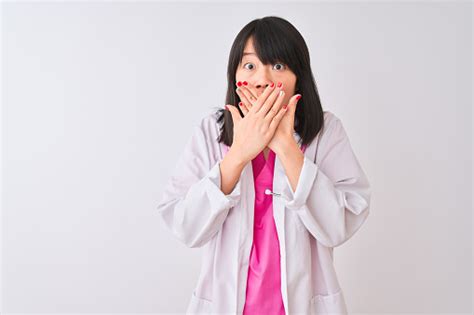 고립 된 흰색 배경 위에 청진기를 입은 젊은 아름다운 중국 의사 여성은 실수로 손으로 입을 덮는 충격을 받았습니다 비밀