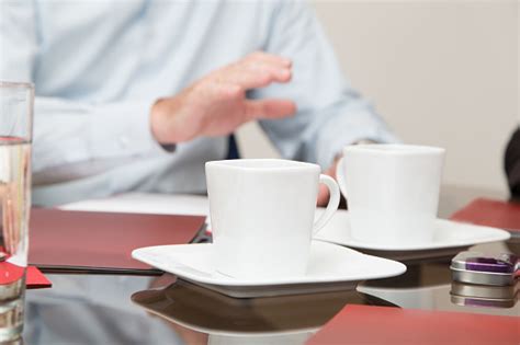 흰색 커피 컵과 접시가있는 유리 테이블 문서 옆에 백그라운드에서 셔츠를 입은 사람 0명에 대한 스톡 사진 및 기타 이미지 0