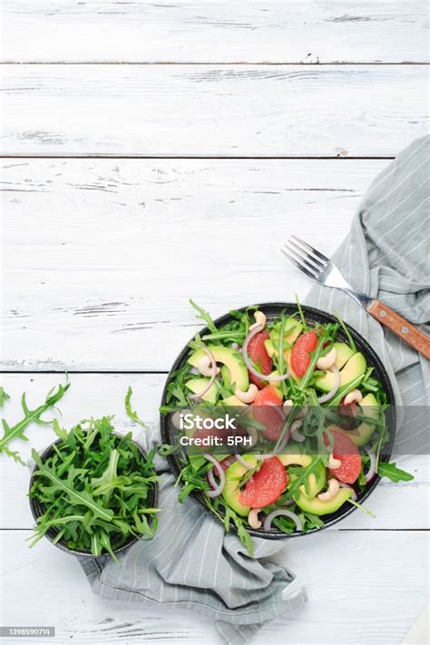 Arugula 아보카도 핑크 자몽 캐슈 너트 및 올리브 오일 꿀 및 와인 식초의 드레싱을 곁들인 건강한 채식주의 자 샐러드 하얀 소박한 부엌 테이블 꼭대기 전망 부정적인