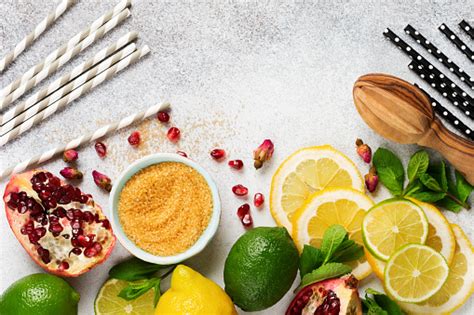 상쾌한 음료 레모네이드 모히토 또는 차가운 상쾌한 차를 위한 요리 배경 신선한 레몬 라임 석류 말린 차 장미 꽃 차 지팡이 설탕 회색 배경에 민트 꽃다발을 남깁니다 감귤류