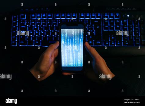 Computer Hacker Hand Holding Mobile Phone Against Computer Keyboard At Office Stock Photo Alamy
