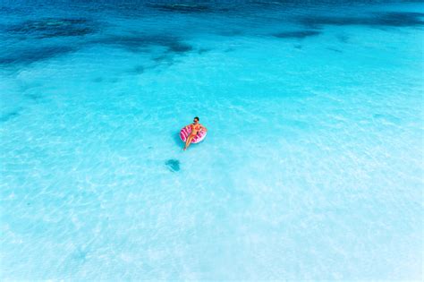 여름에 일몰에 맑고 푸른 바다에서 분홍색 도넛 수영 반지와 함께 수영하는 젊은 여성의 공중 보기 소녀와 열대 공중 풍경 맑은 푸른 물 모래 해변 맨 위 보기 여행 경관에