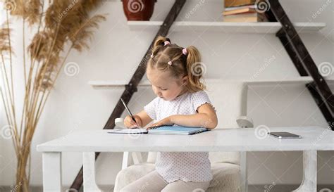 девочка блондинка ученица начальной школы делает домашнее задание у себя за столом дошкольник