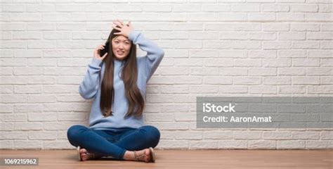 머리 수치심과 깜짝 얼굴로 충격된에 손으로 압박 하는 벽돌 벽을 통해 바닥에 앉아 젊은 중국 여자 화가 좌절 두려워 하 고 실수에 대 한 화가 휴대전화에 대한 스톡 사진 및