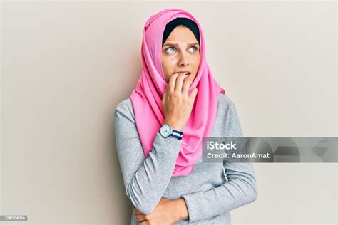 전통적인 이슬람 히잡 스카프를 입은 젊은 백인 여성은 손톱을 물고 입에 손을 대고 스트레스와 긴장한 표정을 짓고 있습니다 불안 문제 감정에 대한 스톡 사진 및 기타 이미지