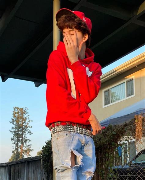 A Boy In A Red Hoodie And Ripped Jeans Covers His Face