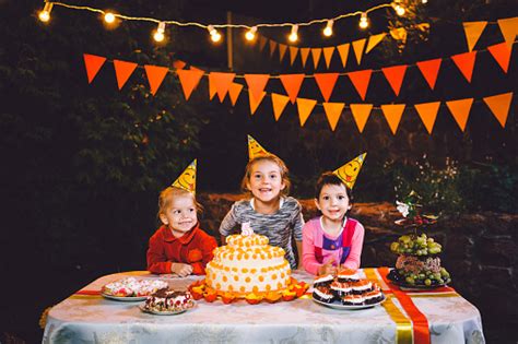 어린이 생일 파티 그들의 손으로 케이크를 먹고 그들의 얼굴에 바르는 테이블에서 3 쾌활 한 아이 여자 재미와 밝은 전구 장식된 안뜰 Décor에 축제 분위기 가꿔주기에 대한