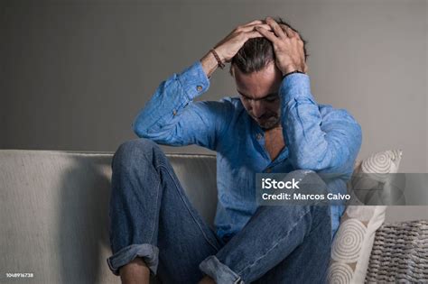 라이프 스타일 초상화의 매력적이 고 잘생긴 젊은 라틴 사람 앉아 피곤 하 고 집에서 우울 소파 소파 느낌 압도 하 고 걱정 하는 우울증 위기와 불안 문제를 겪고 슬픈 감정에