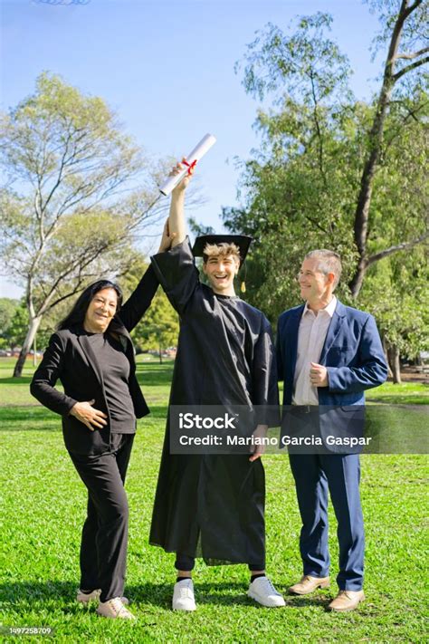최근에 졸업한 소년은 모자와 가운을 입고 학위를 손에 들고 대학 캠퍼스에서 다민족 가족과 함께 축하합니다 매우 행복한 표현 성취