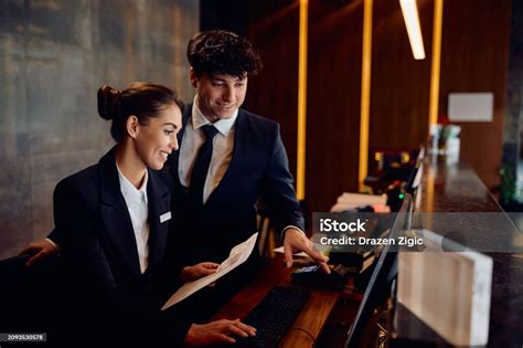 호텔 프론트 데스크에서 컴퓨터 작업을 하면서 협력하는 행복한 접수원 호텔에 대한 스톡 사진 및 기타 이미지 호텔 호텔 리셉션 호텔 관련 직업 Istock