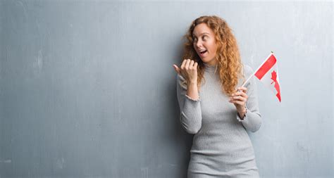 캐나다의 국기를 들고 회색 그런 지 벽에 젊은 빨강 머리 여자는 고 행복 얼굴 웃 고 옆까지 엄지 표시 가리키기에 대한 스톡 사진 및 기타 이미지 Istock