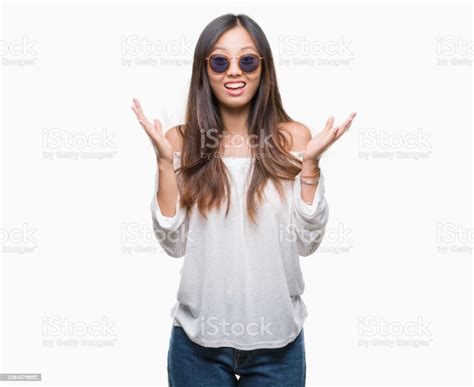 위에 선글라스를 착용 하는 젊은 아시아 여성 격리 배경 미친을 축 하 하 고 무기와 성공을 위한 흥분 비명 제기 및 오픈 눈 깜짝 놀라게 우승자 개념 긍정적인 감정 표현에