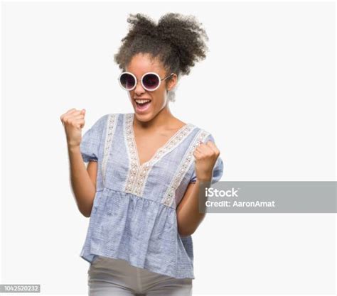 젊은 아프리카 미국 여자 매우 행복 하 고 흥분 무기와 우승자 제스처를 하 고 격리 된 배경 위에 안경을 쓰고 웃 고 성공을