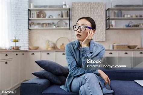 거실의 소파에 앉아있는 안경을 쓰고 생각하는 젊은 아름다운 아시아 여성 20 24세에 대한 스톡 사진 및 기타 이미지 20 24세 가정 생활 걱정하는 Istock