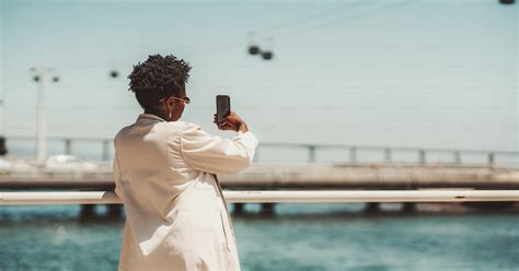 곱슬 곱슬 한 아프리카 머리 흰색 트렌치와 곱슬 머리 머리를 가진 젊은 흑인 여성 관광객의 뒤에서 관광과 물 위의 로프웨이 사진을 찍는 모습 오른쪽의 복사 공간 사진