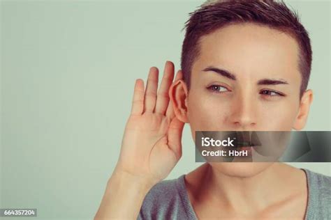 여 자가 가까이 귀 및 수신 회색 벽 바탕에 신중 하 게 고립 된 그녀의 손을 보유 하고있다 인간의 감정이 신체 언어 얼굴 얼굴 표현 감각 지각에 대한 스톡 사진 및 기타