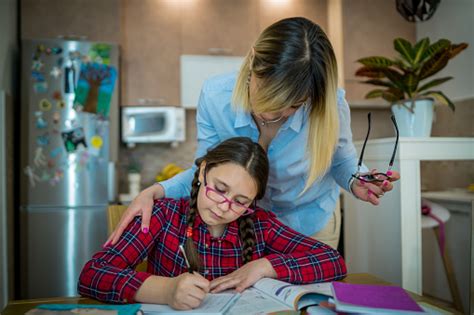 매력적인 젊은 여성과 그녀의 작은 귀여운 딸은 테이블에 앉아 함께 숙제를하고있습니다 어머니는 딸이 학교 수업을 하도록 도와줍니다 2명에 대한 스톡 사진 및 기타 이미지