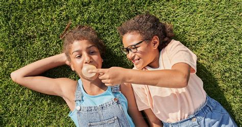 야외에서 여자 친구의 껌을 깨는 어린 소녀 어린 시절의 개념 우정의 아이디어 현대 아이 라이프 스타일 푸른 잔디에 누워 농담 곱슬 갈색 머리 소녀 사진