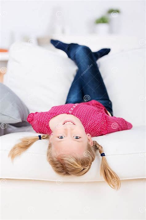 Усмехаясь лежать девушки вверх ногами на софе Стоковое Изображение изображение насчитывающей